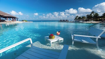 Piscina azul límpida com espreguiçadeiras e paisagem tropical.