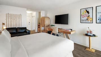 Quarto de hotel moderno com uma cama grande, uma escrivaninha, uma cadeira, uma TV e um quadro na parede.