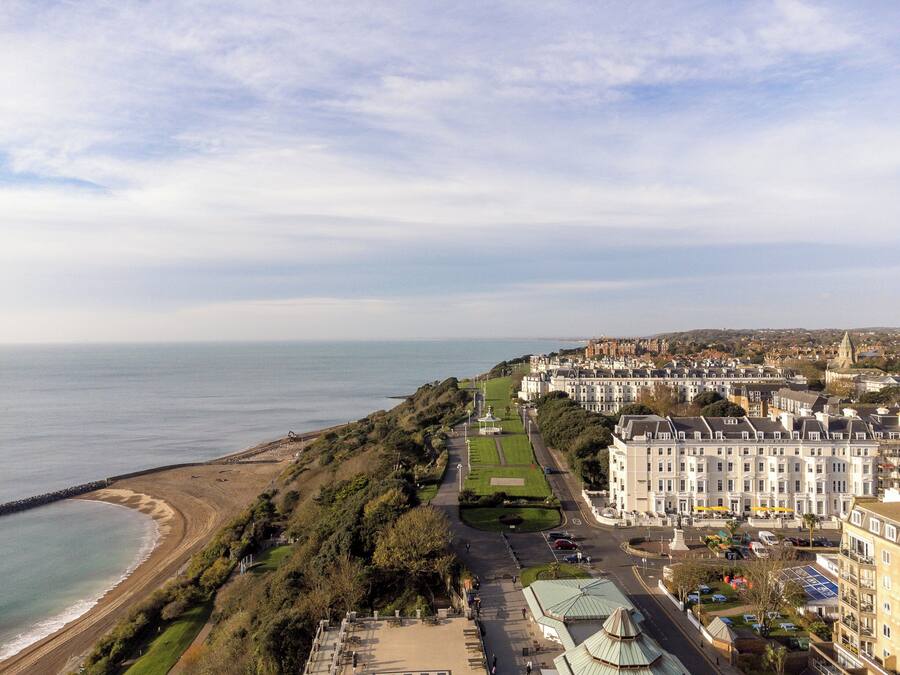 Uma vila costeira com calçadão, edifícios e vista para o mar.