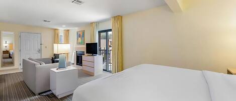 Quarto de hotel com cama, escrivaninha com cadeira, televisão e uma janela grande com cortinas.