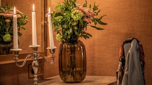 Um banheiro com espelho, um vaso de flores e duas velas acesas.