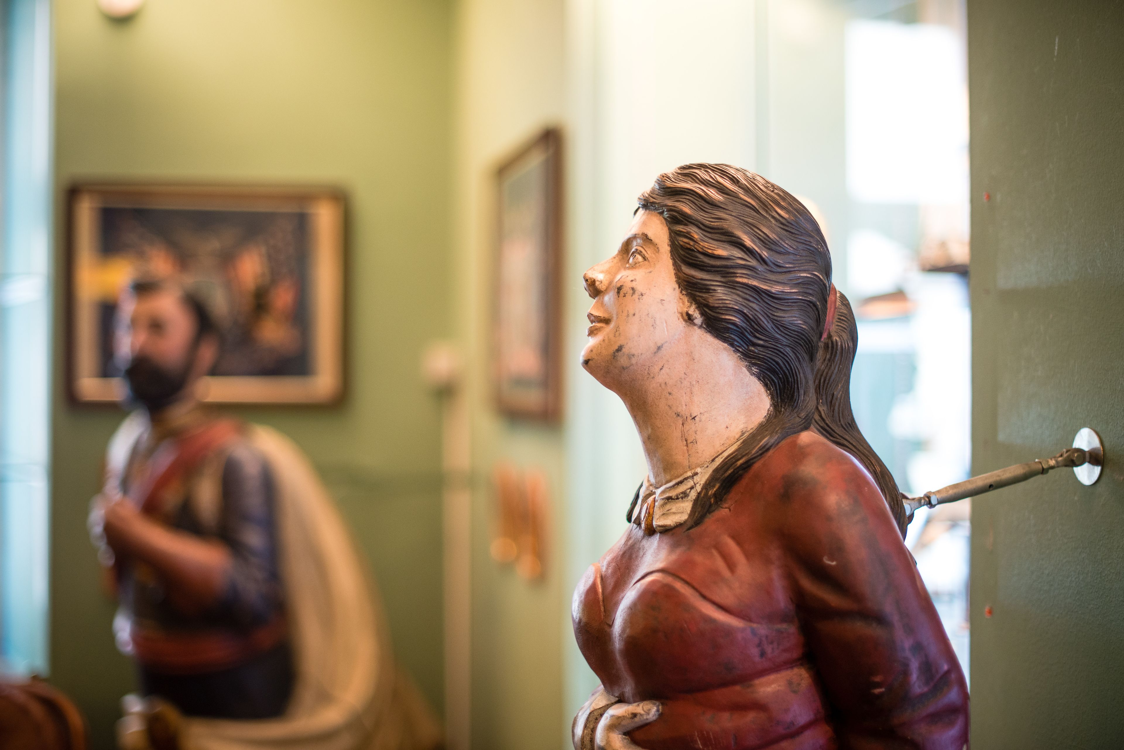 Uma estátua de uma pessoa com uma espada, um espelho e um quadro emoldurado na parede.