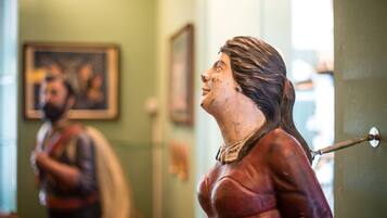 Uma estátua de uma pessoa com uma espada, um espelho e um quadro emoldurado na parede.