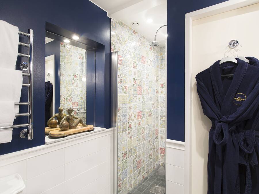 Casa de banho com parede azul, chuveiro com azulejos coloridos, pia branca e um roupão pendurado num suporte.
