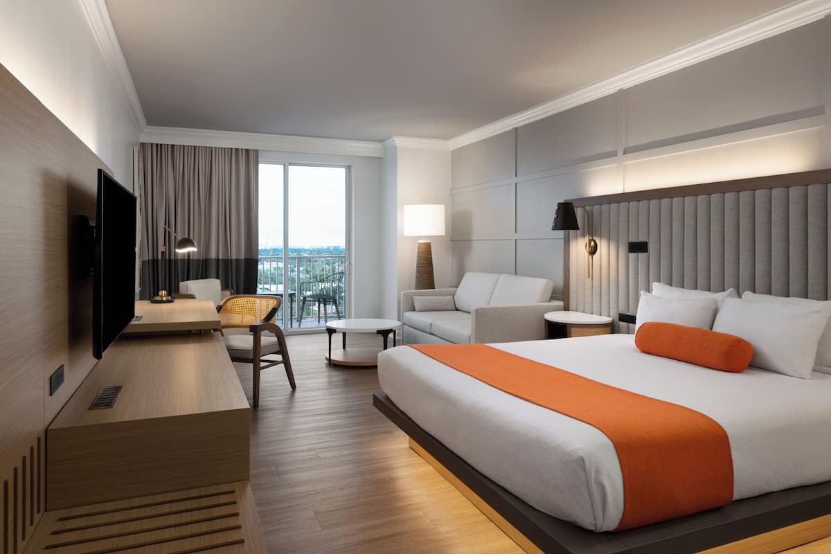 Quarto de hotel moderno com uma cama grande, um sofá, uma escrivaninha e uma televisão.