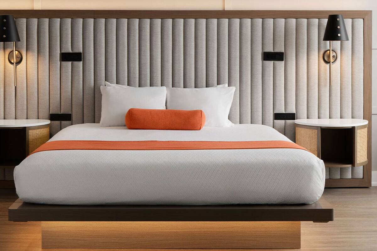Uma cama com cabeceira, duas mesas de cabeceira e duas luminárias fixadas na parede.