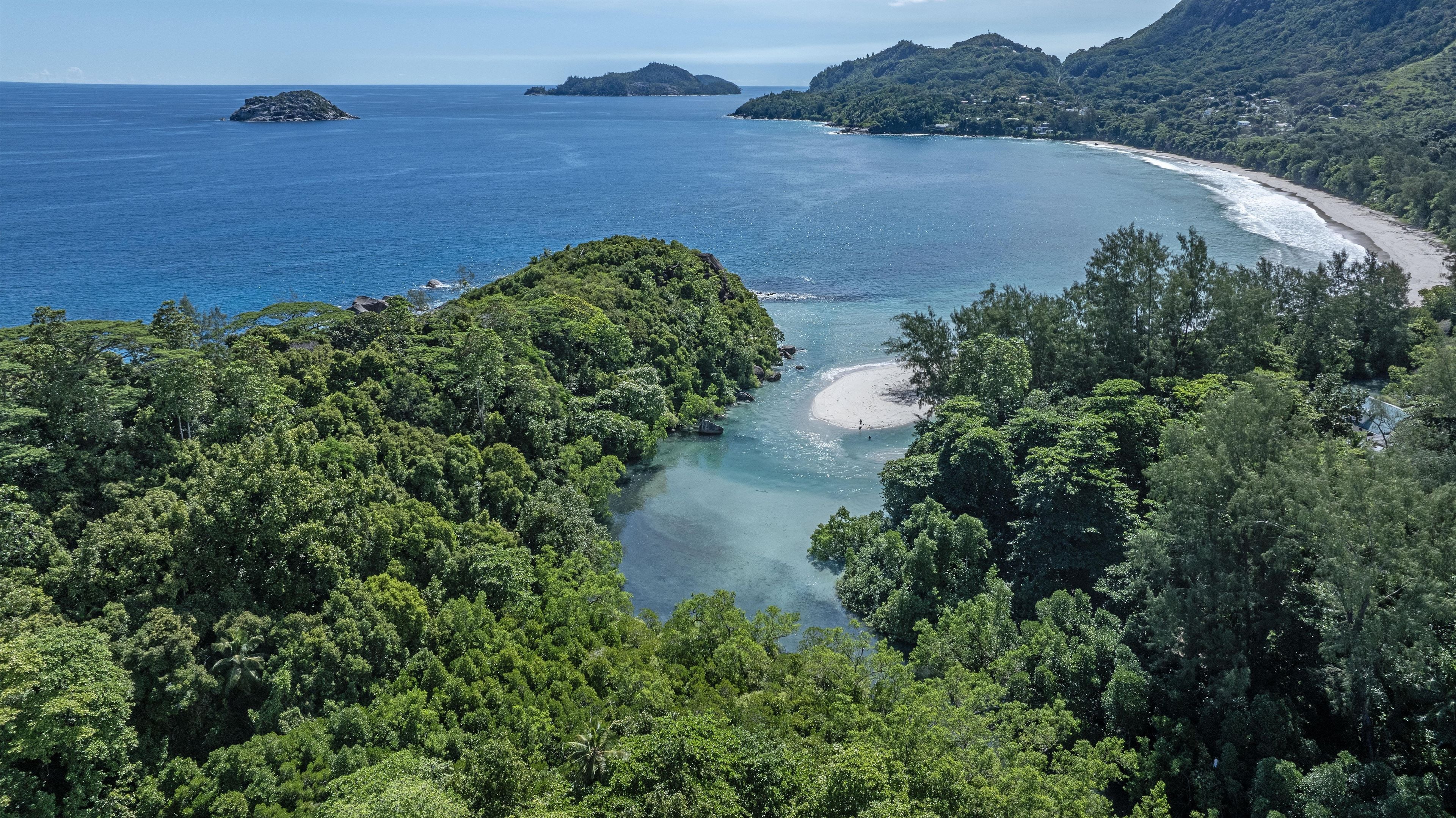 Paisagem costeira com praia, áreas arborizadas e águas azul-claras.