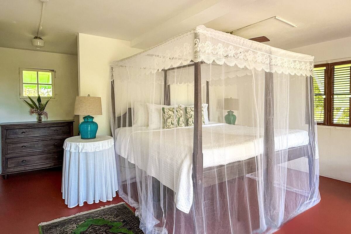 Um quarto com uma cama de dossel, uma mesinha de cabeceira, um abajur e uma janela com persianas.