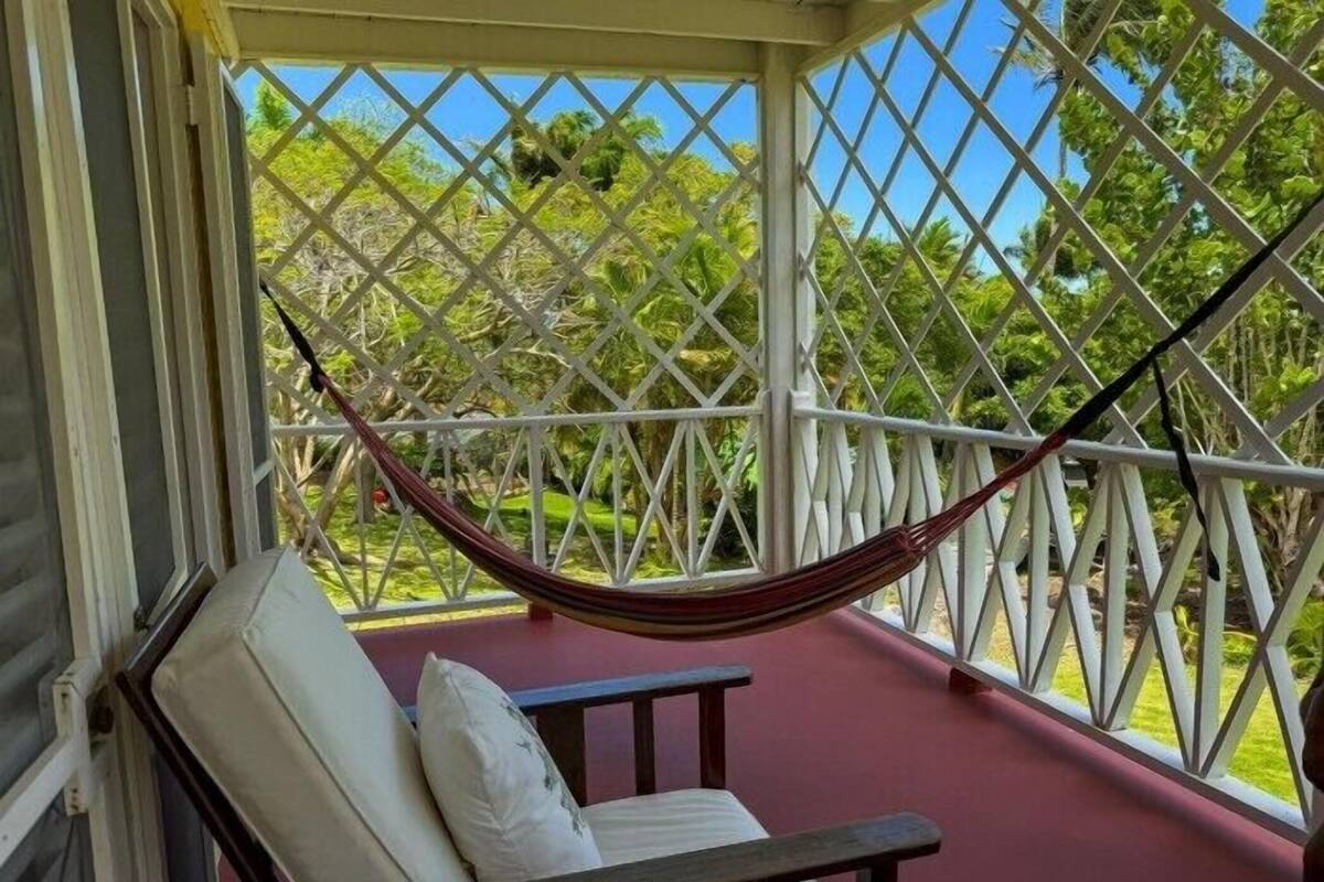 Uma cadeira de rede numa varanda com vista para um jardim e árvores.
