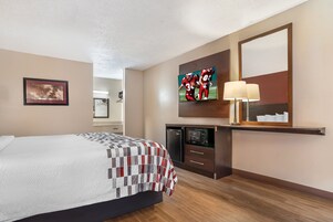 Quarto de hotel com cama, televisão de tela plana, escrivaninha com abajur e espelho.