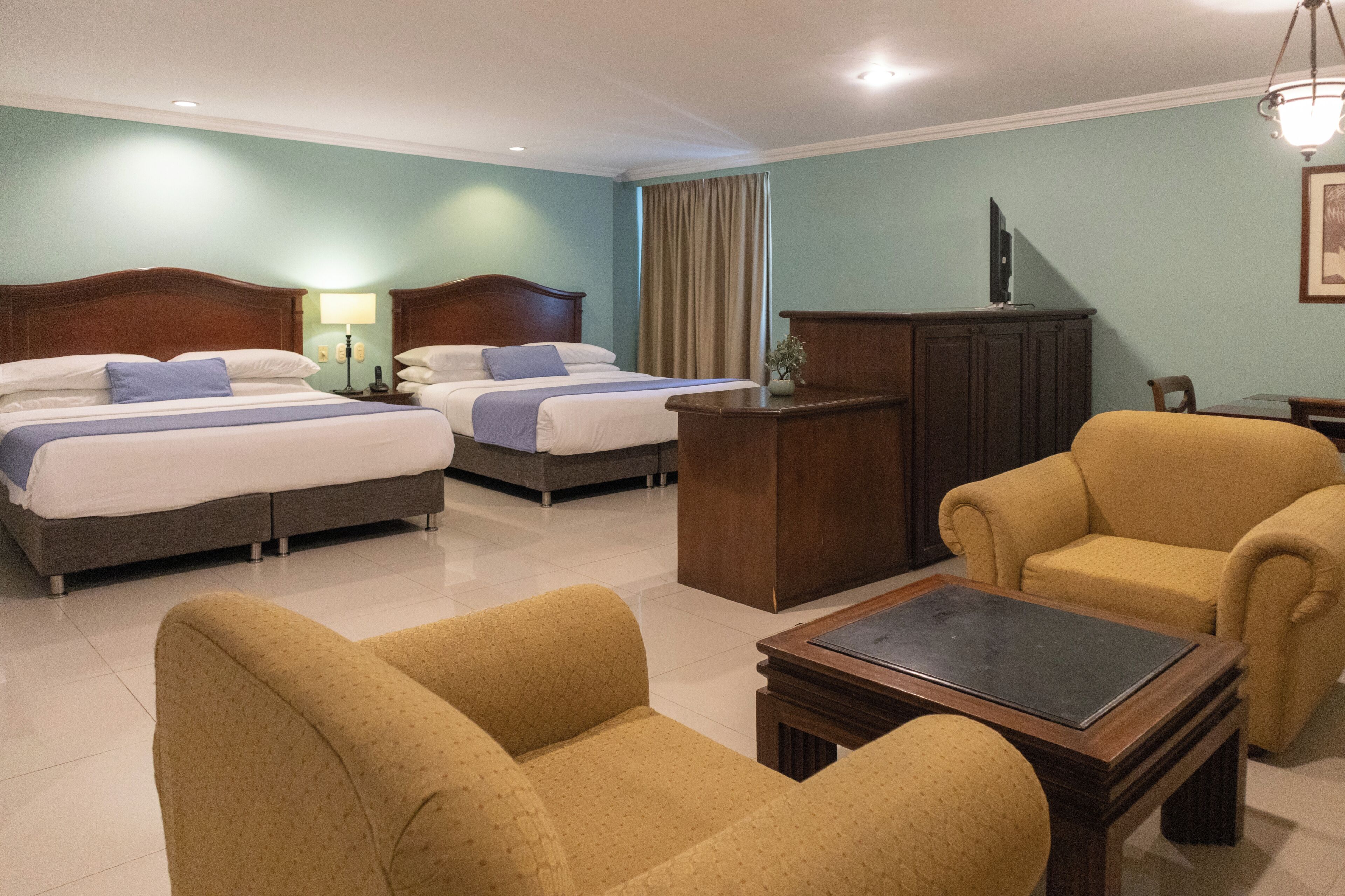 Quarto de hotel com duas camas, uma escrivaninha, uma cadeira e um sofá.