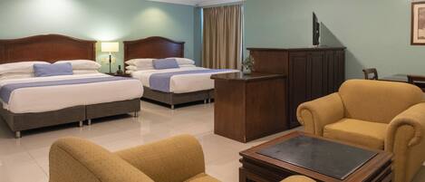 Quarto de hotel com duas camas, uma escrivaninha, uma cadeira e um sofá.