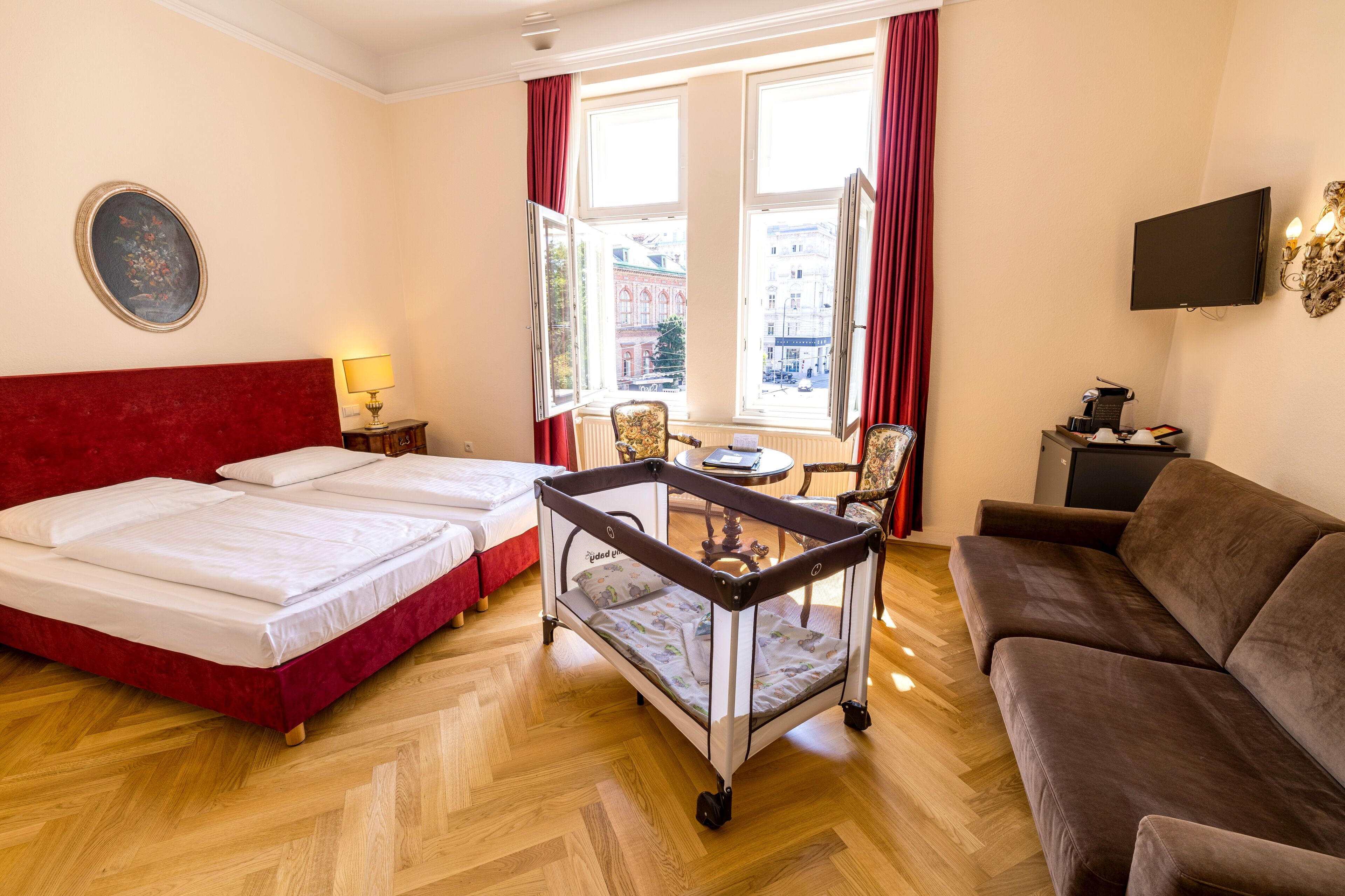 Quarto de hotel com duas camas, um sofá, uma mesa pequena e uma televisão.