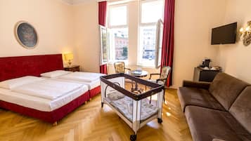 Quarto de hotel com duas camas, um sofá, uma mesa pequena e uma televisão.