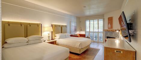 Quarto de hotel com duas camas, uma mesa de trabalho, televisão e janela com persianas.