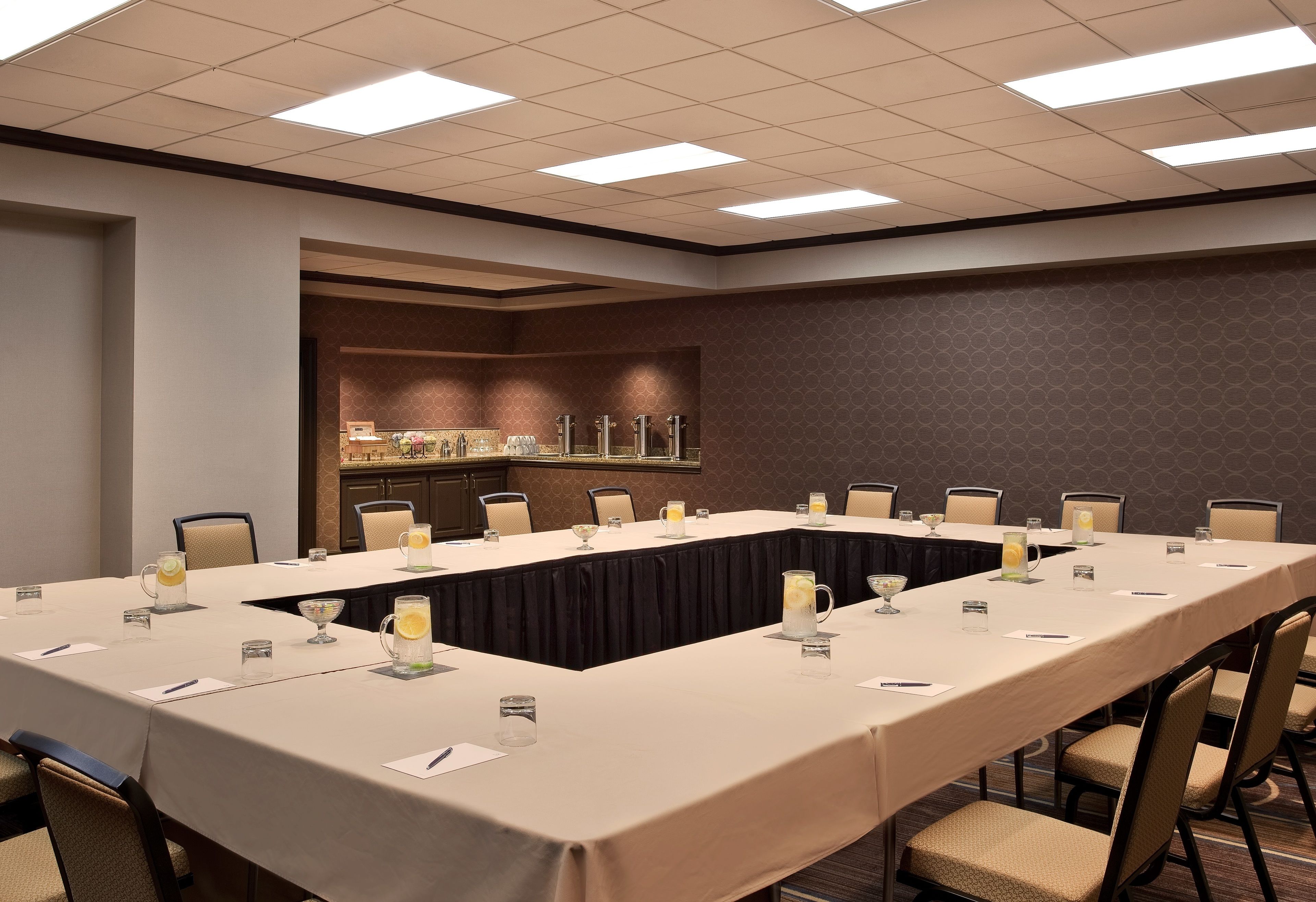 Uma sala de conferências com uma mesa comprida, cadeiras e um bar ao fundo.