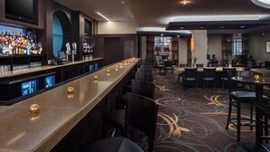 Uma área de bar com um balcão extenso, diversas opções de assento e piso coberto por carpete.