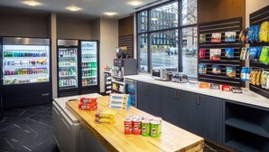 Espaço de serviço com máquinas de bebidas refrigeradas, micro-ondas e uma seleção de snacks e bebidas nas prateleiras.