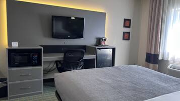 Quarto de hotel com cama, escrivaninha com computador, micro-ondas, cadeira e televisão.