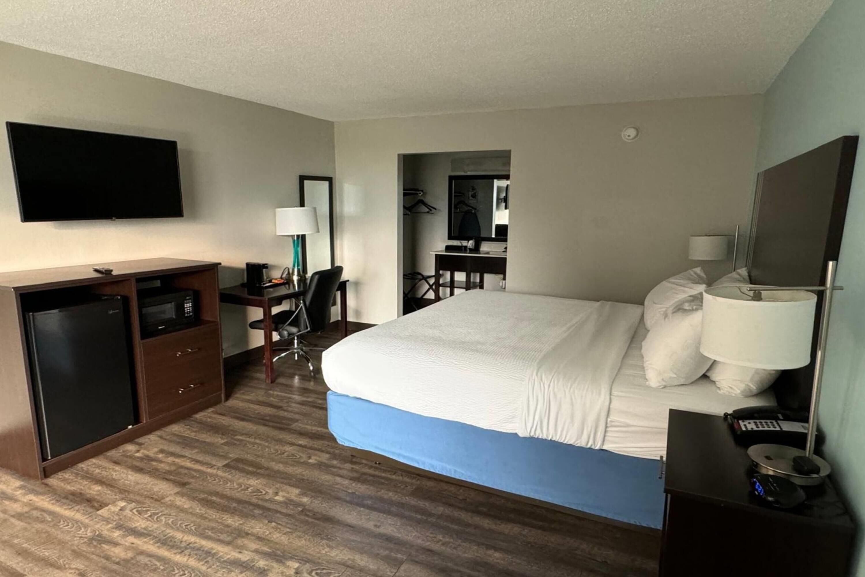 Quarto de hotel com cama, escrivaninha, cadeira, televisão e pequeno frigorífico.