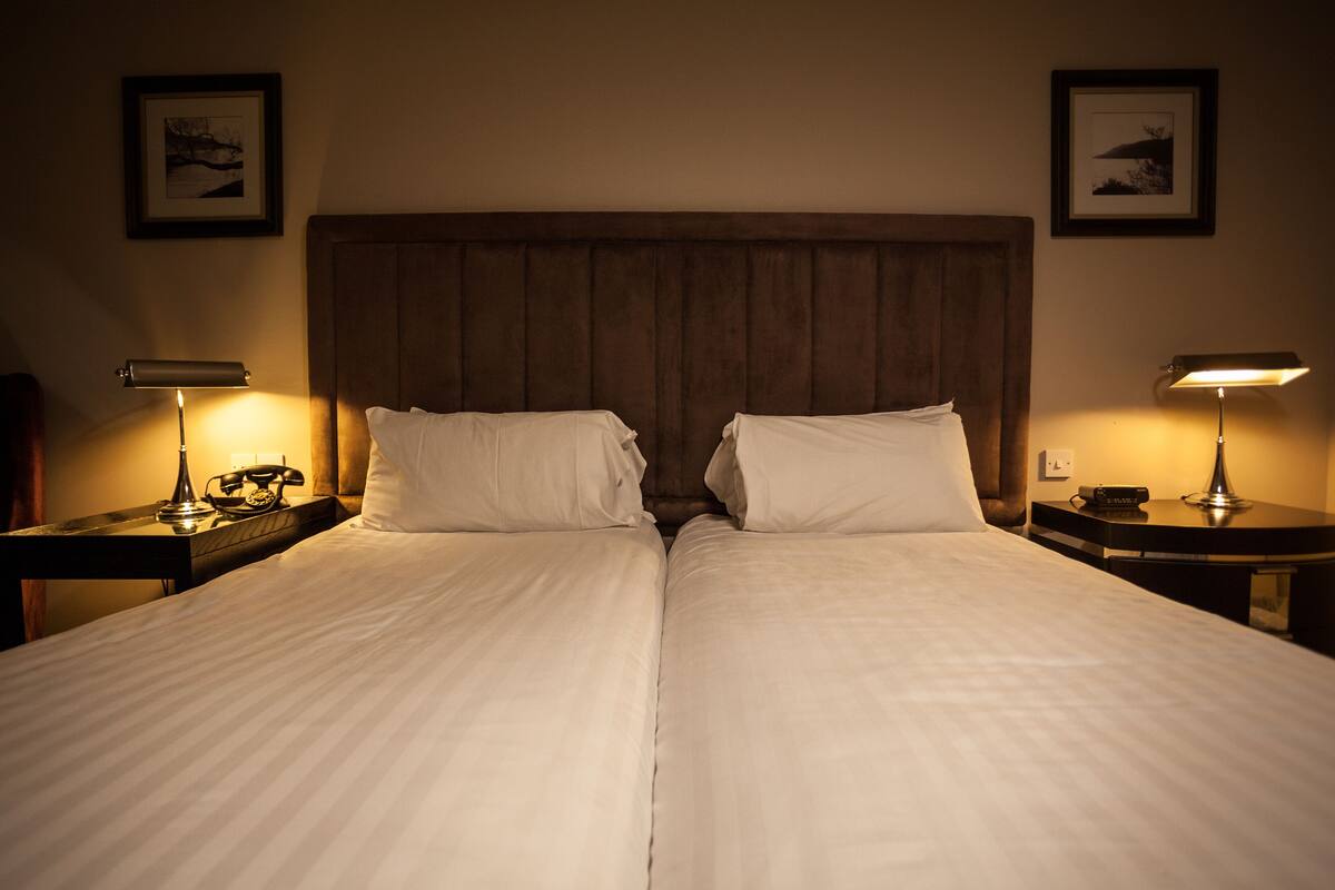 Uma cama de casal com cabeceira de madeira, duas mesas de cabeceira com abajures e quadros nas paredes.
