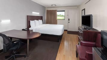 Quarto de hotel com cama, escrivaninha, cadeira, televisão e janela com cortinas.