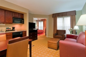 Quarto de hotel com cozinha compacta, televisão, sofá, poltrona e cama.