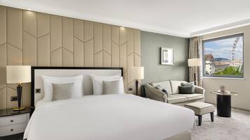 Quarto de hotel com uma cama grande, duas mesas de cabeceira, um sofá, uma mesinha e uma janela vista para uma roda gigante.