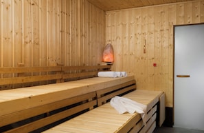 Uma sala de sauna de madeira com bancos, pedra aquecida e uma porta.