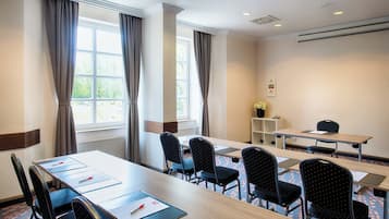 Uma sala de conferência com uma mesa comprida, cadeiras e uma mesinha lateral com um vaso.