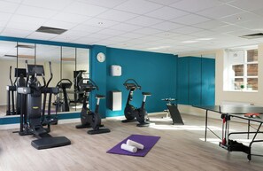 Uma academia com equipamentos de exercícios, um espelho, um relógio e uma janela.