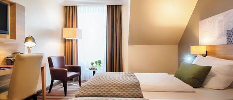 Quarto de hotel com duas camas, uma escrivaninha, uma cadeira, um abajur e uma janela com cortinas.