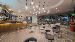 Espaço lounge moderno com assentos, bar e amplas janelas com vista para a cidade.