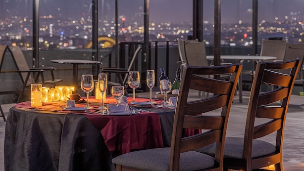 Mesa posta para refeição com vista para a cidade, incluindo toalha, cadeiras e velas acesas.