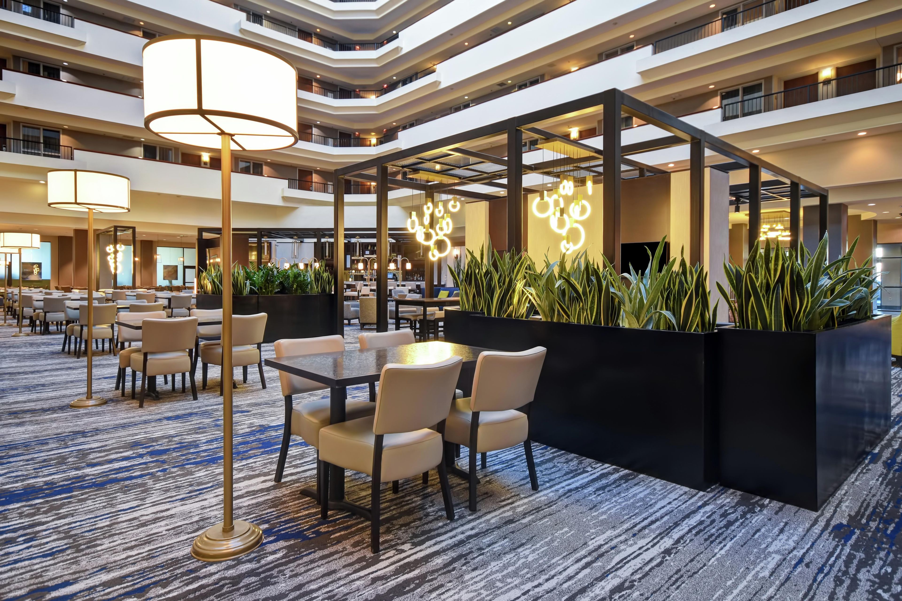 Um hall de hotel com vários níveis, com área de estar central, um bar e uma escadaria.