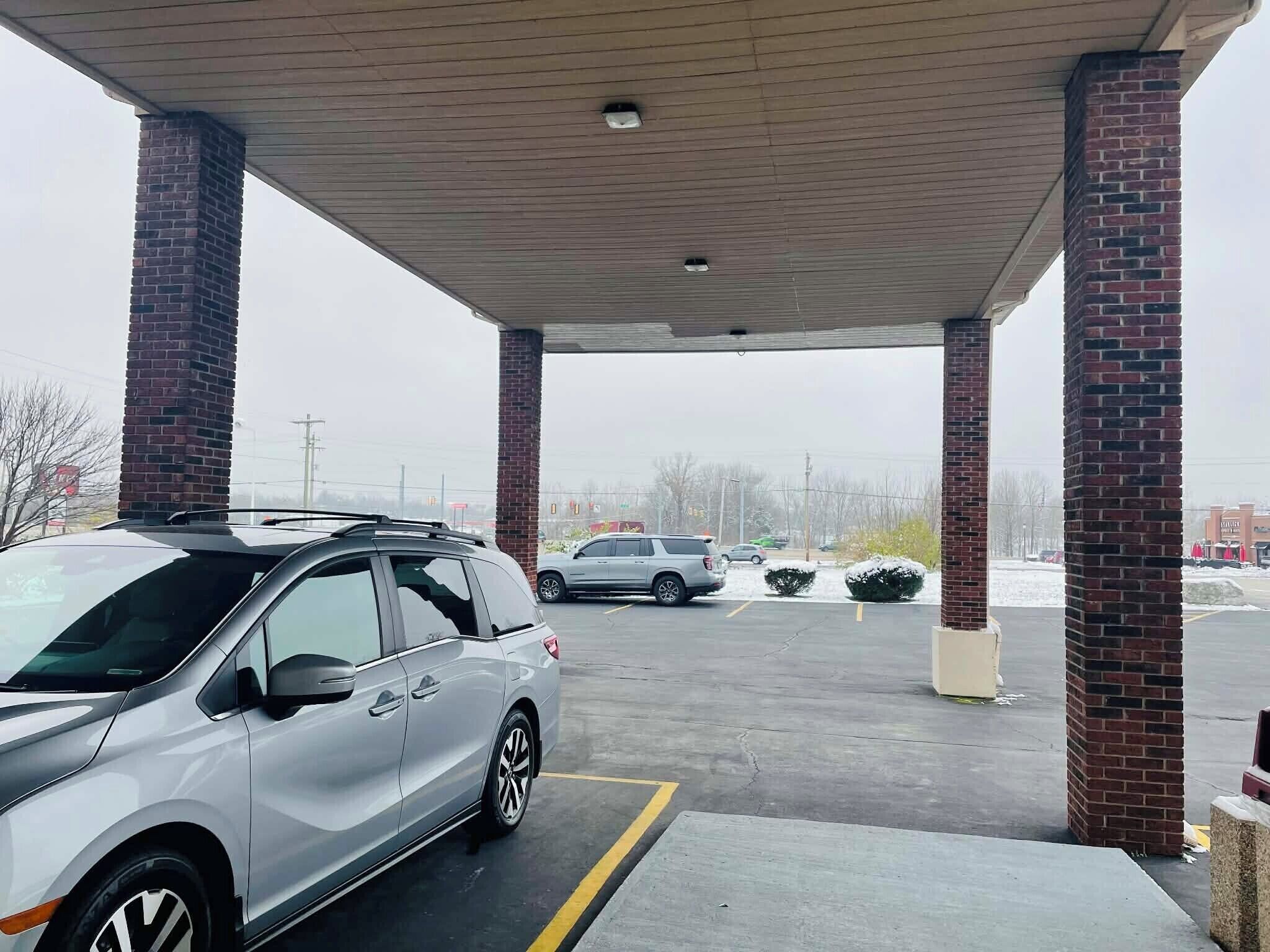 Uma área de estacionamento coberta com pilares de tijolo, um SUV cinza e alguns outros veículos.