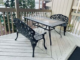 Um deck de madeira com uma mesa e cadeiras de metal, cercado por uma cerca de madeira.