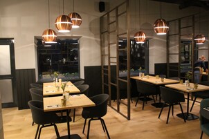 Interior de restaurante moderno com mesas de madeira, cadeiras pretas e iluminação pendente em cobre.