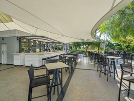 Café ao ar livre com área de bar, mesas e cadeiras dispostas sob um toldo.