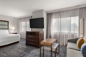 Quarto de hotel com cama, televisão, escrivaninha, poltrona e sofá.