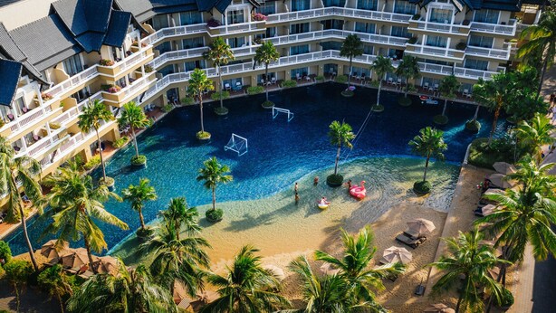 Resort com várias varandas, piscina central e área de praia com espreguiçadeiras e guarda-sóis.