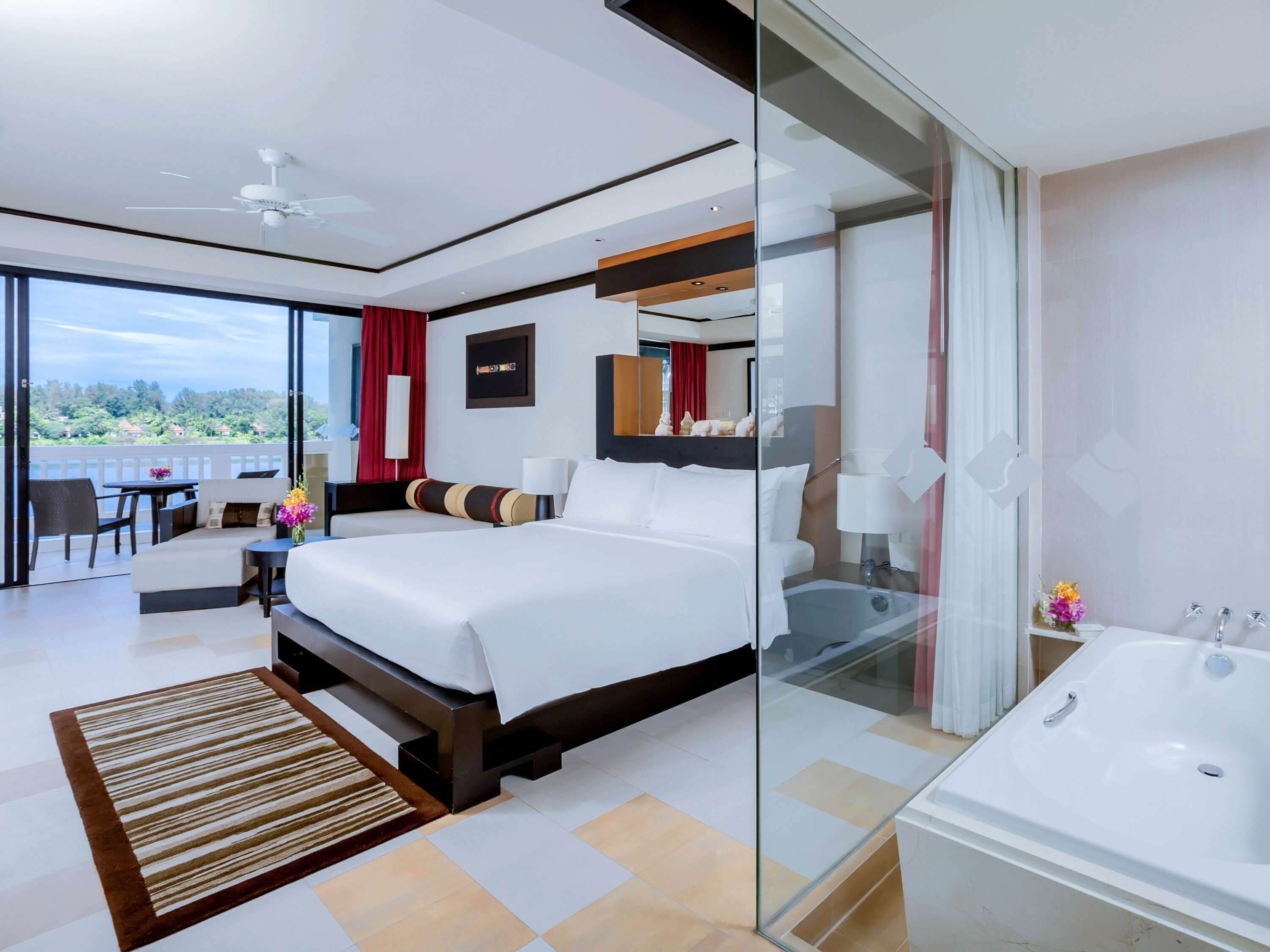 Quarto de hotel moderno com uma cama grande, banheiro com paredes de vidro, varanda com vista e área de jantar.