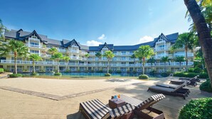 Resort com edifícios de vários andares, piscina e espreguiçadeiras numa área de areia.