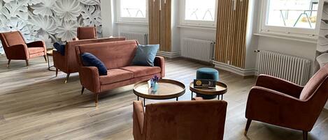 Uma sala de estar moderna com um sofá, poltronas e uma mesa de centro. Há janelas com vista para áreas verdes.