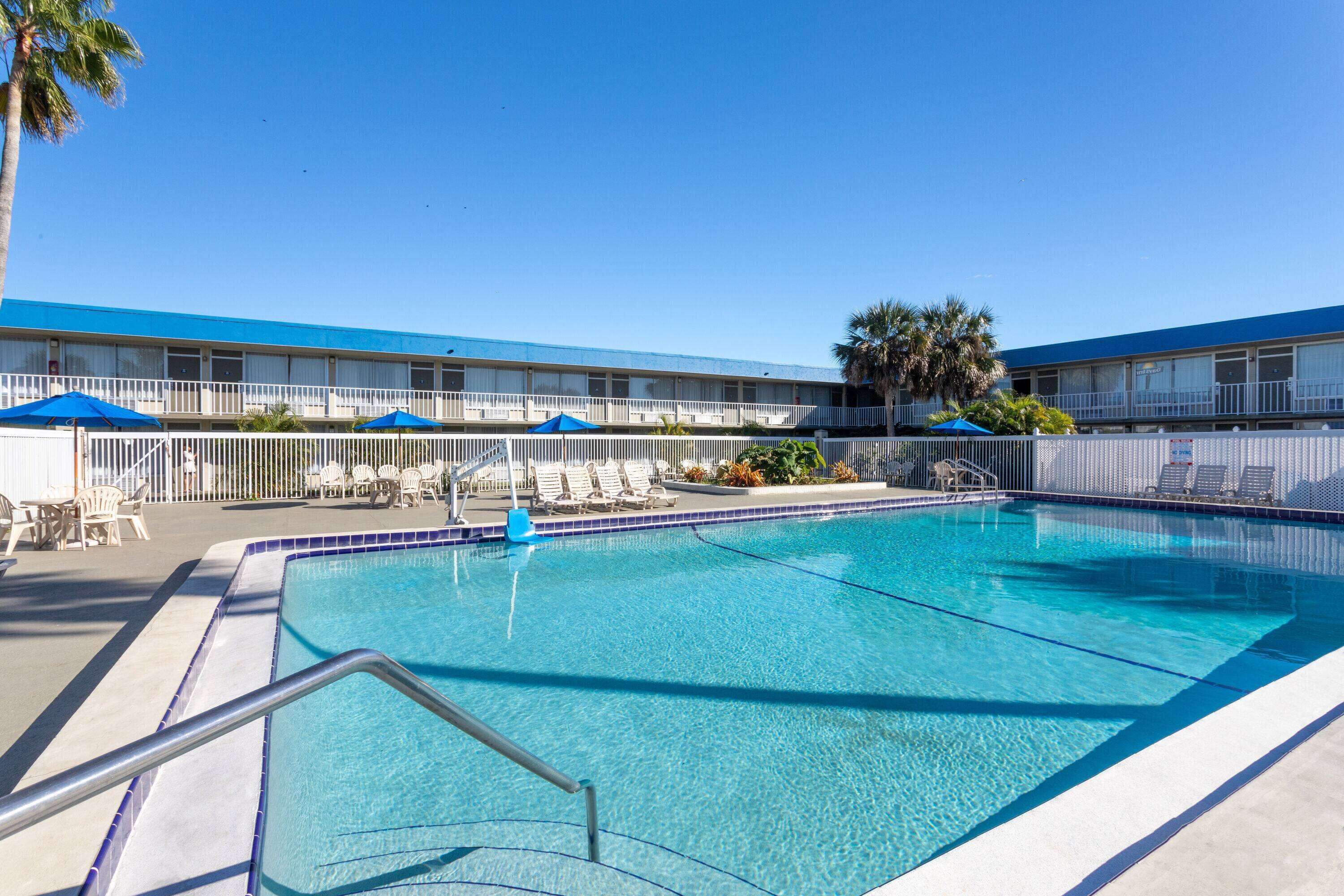 Piscina com escada de metal, espreguiçadeiras e guarda-sóis.