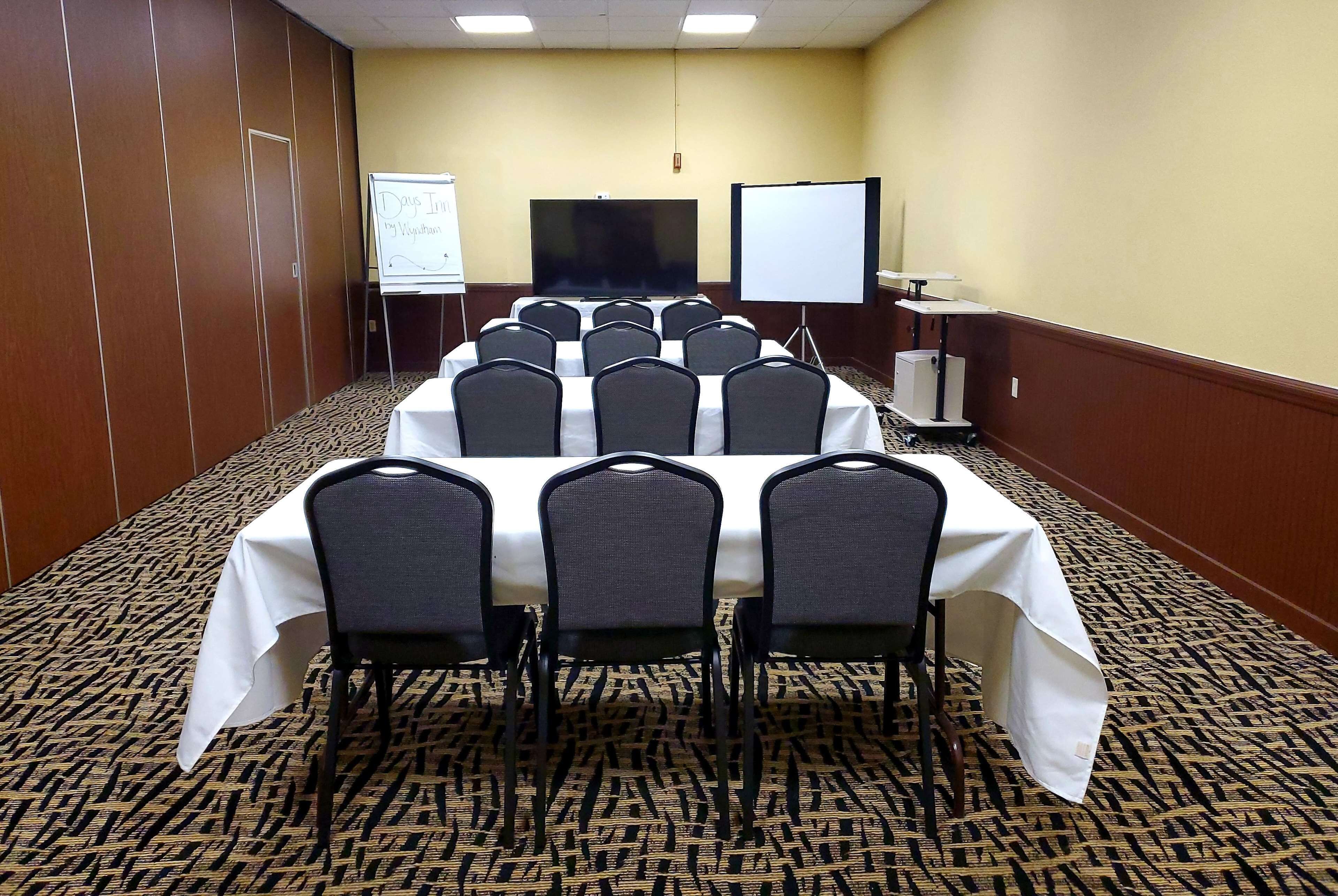Uma sala de conferência com uma mesa comprida, várias cadeiras, um quadro branco e um projetor.
