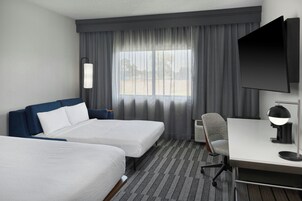 Quarto de hotel com duas camas, uma escrivaninha, uma cadeira, uma televisão e uma janela com cortinas.