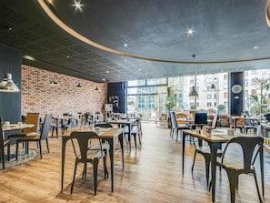 Um café espaçoso com mesas e cadeiras de madeira, parede de tijolos e amplas janelas com vista para a cidade.