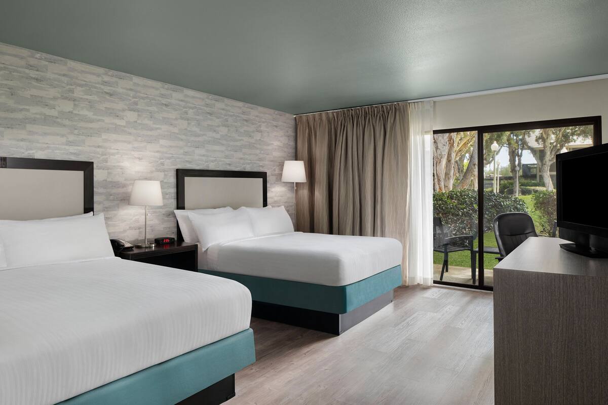 Quarto de hotel com duas camas, televisão e vista para o exterior.