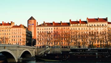 Uma ponte histórica com arco de pedra, um rio e uma fileira de edifícios europeus tradicionais com telhados vermelhos.
